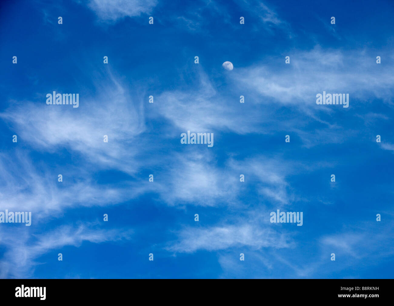 The moon shows through wispy cirrus clouds against a blue sky Stock ...