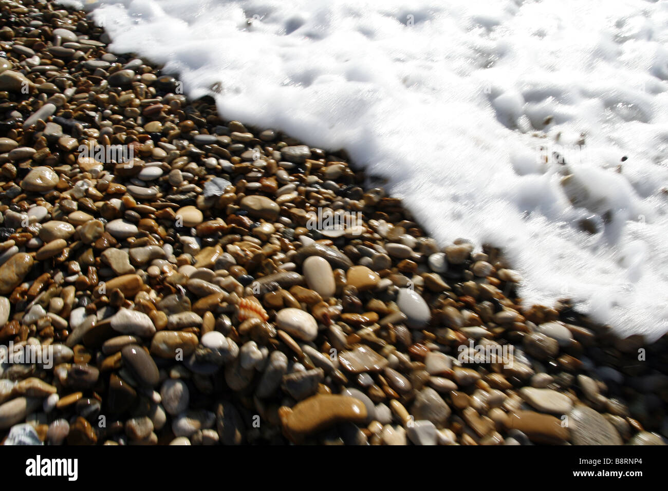 fast flowing ocean wave and sea shells and pebbles washed up on sandy ...