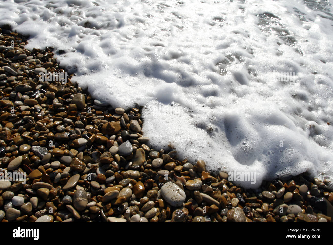 fast flowing ocean wave and sea shells and pebbles washed up on sandy ...