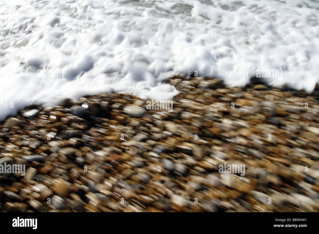 fast flowing ocean wave and sea shells and pebbles washed up on sandy ...