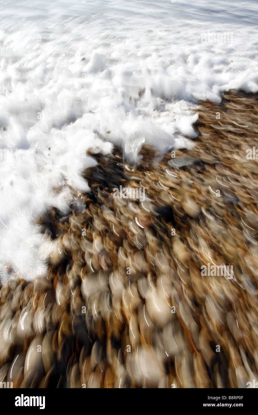 fast flowing ocean wave and sea shells and pebbles washed up on sandy ...