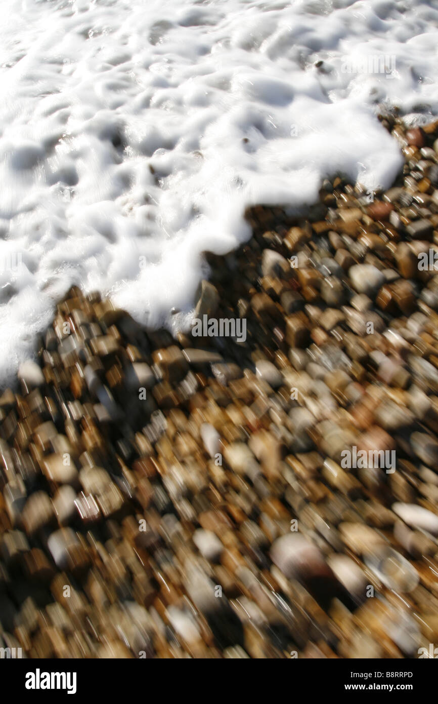 fast flowing ocean wave and sea shells and pebbles washed up on sandy ...