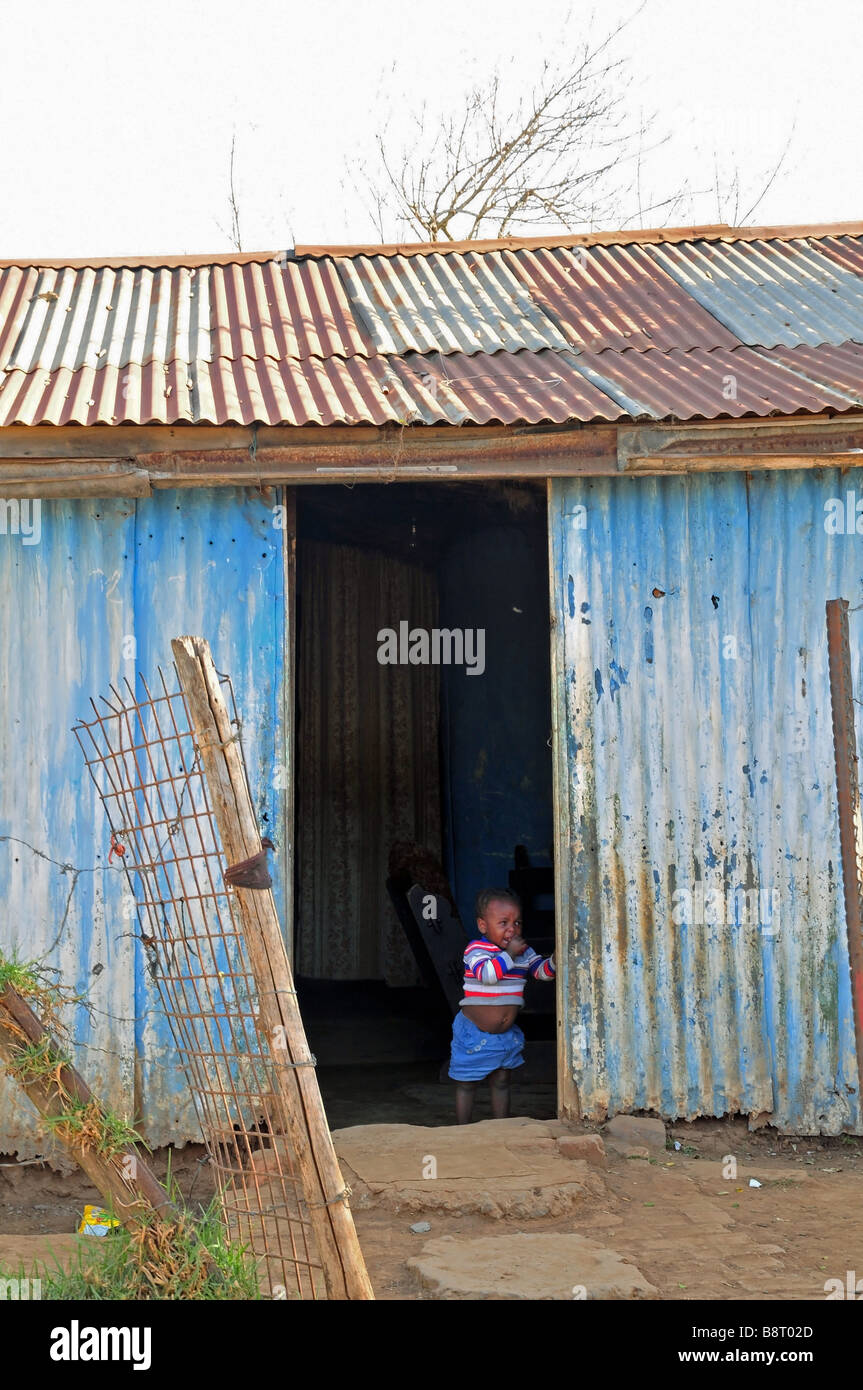 Portrait of a boy toddler standing in the open doorway of a tin shack ...