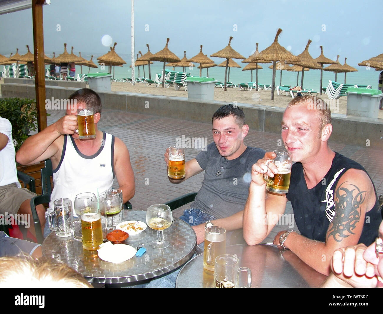 three young men sitting at beach-front promenade and drinking beer ...