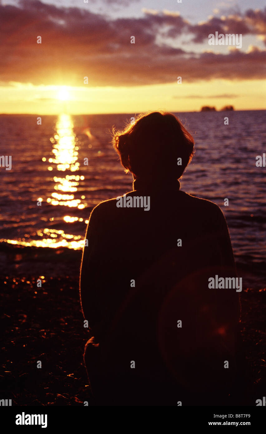 A woman sitting on a beach watching the sun go down Stock Photo - Alamy