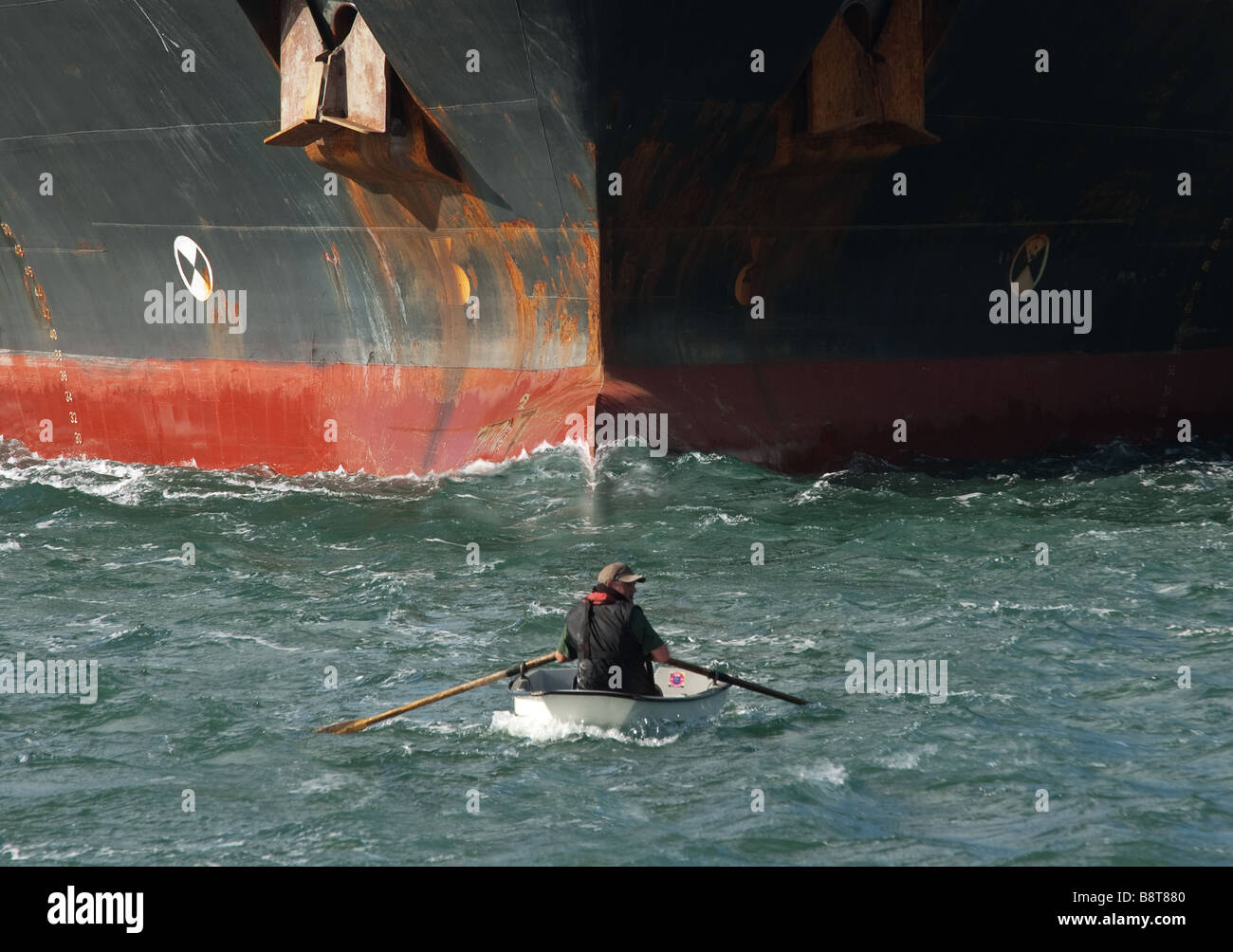 Ship dwarfs a dinghy. Rowing against all the odds Stock Photo - Alamy