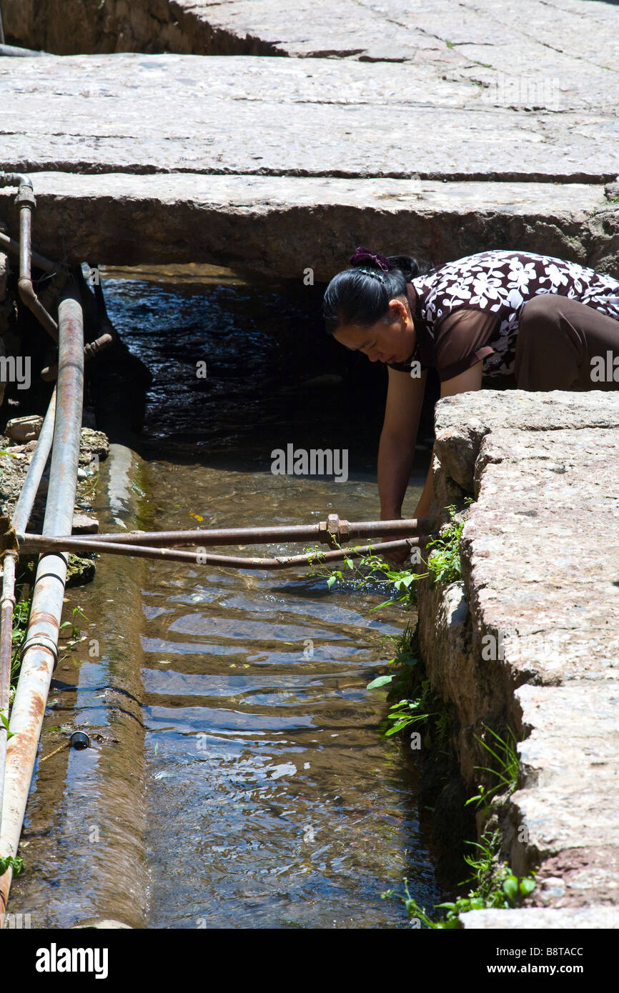 A woman washing clothes in a streetside gutter in Lijiang, Yunnan ...