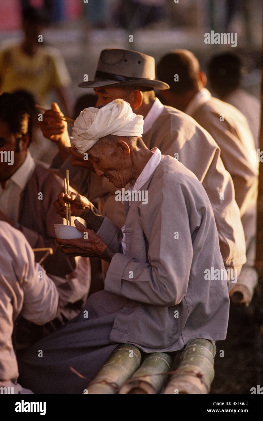 Shan men eating noodles at a street food stall Namhkan Shan State Burma ...
