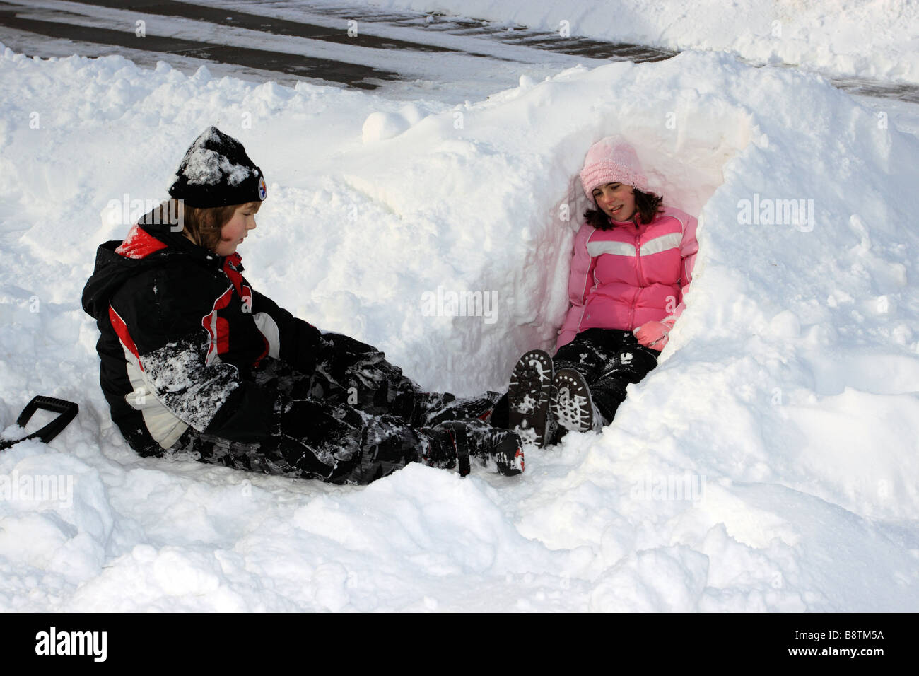 Ten year old boy and twelve year old girl sitting in a snow fort cut ...