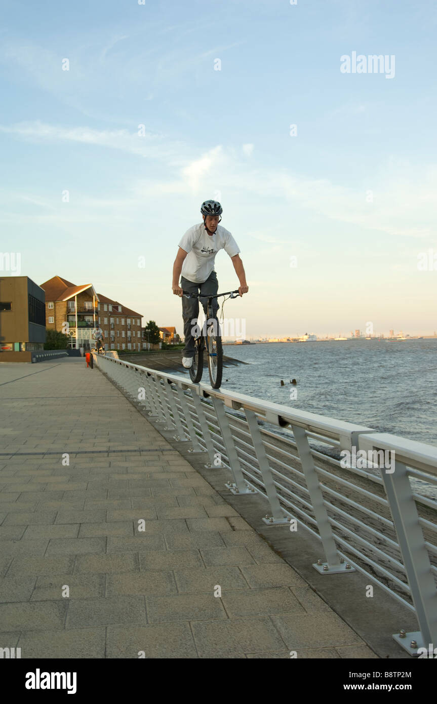 Boy riding mountain bike along top of waterfront handrail by river ...