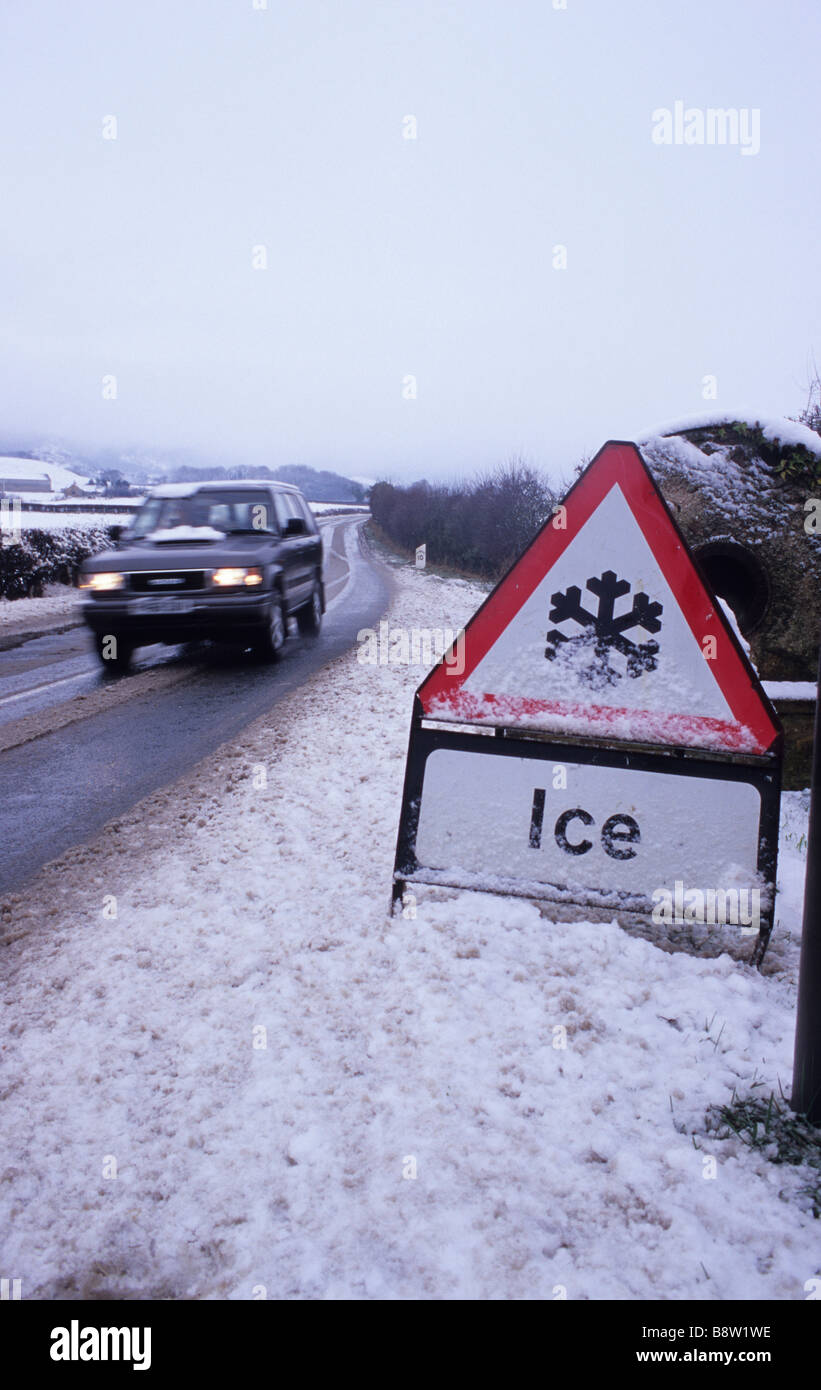 car travelling in winter snow passing warning sign of icy road near ...