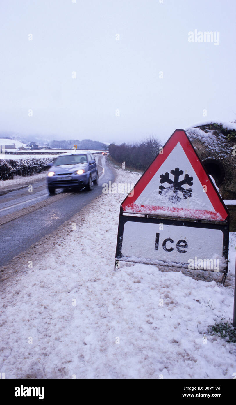 car travelling in winter snow passing warning sign of icy road near ...