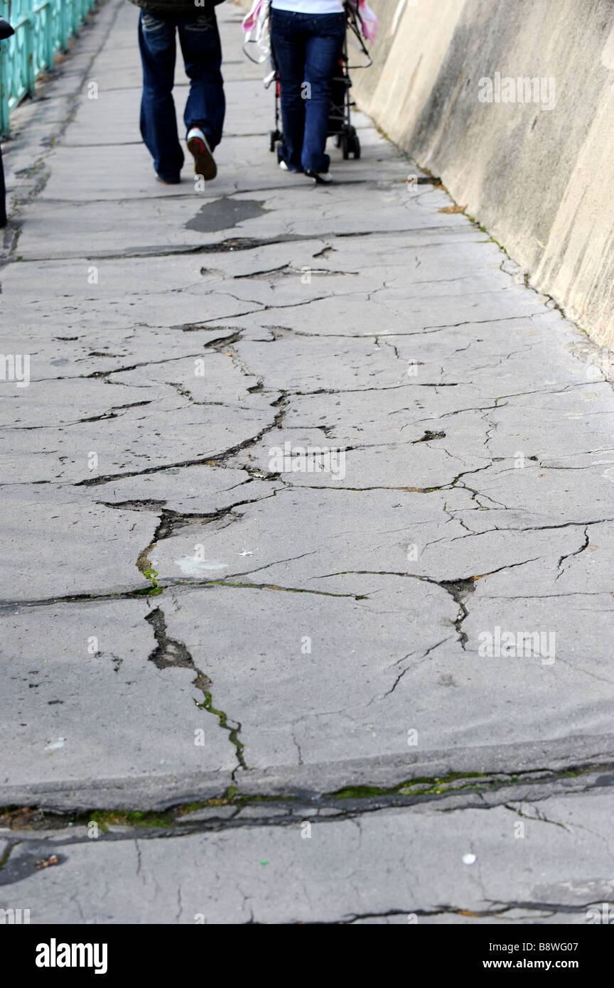 Two people walk on a cracked pavement on a Brighton seafront walkway ...
