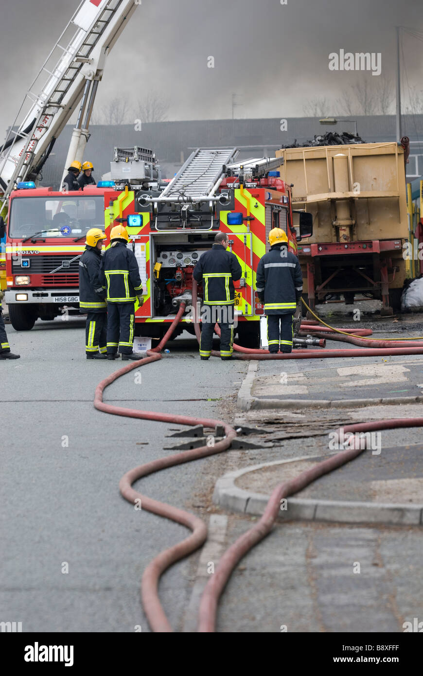 Firefighters at rear of fire engine showing hose in foreground and ...
