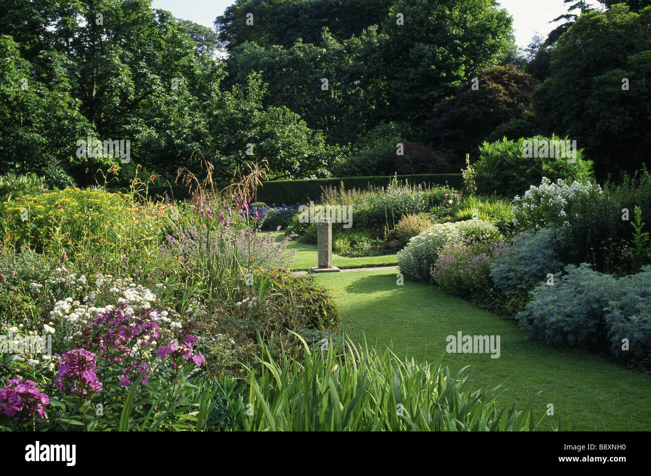 Grass pathway through the herbaceous border with a sundial in the ...