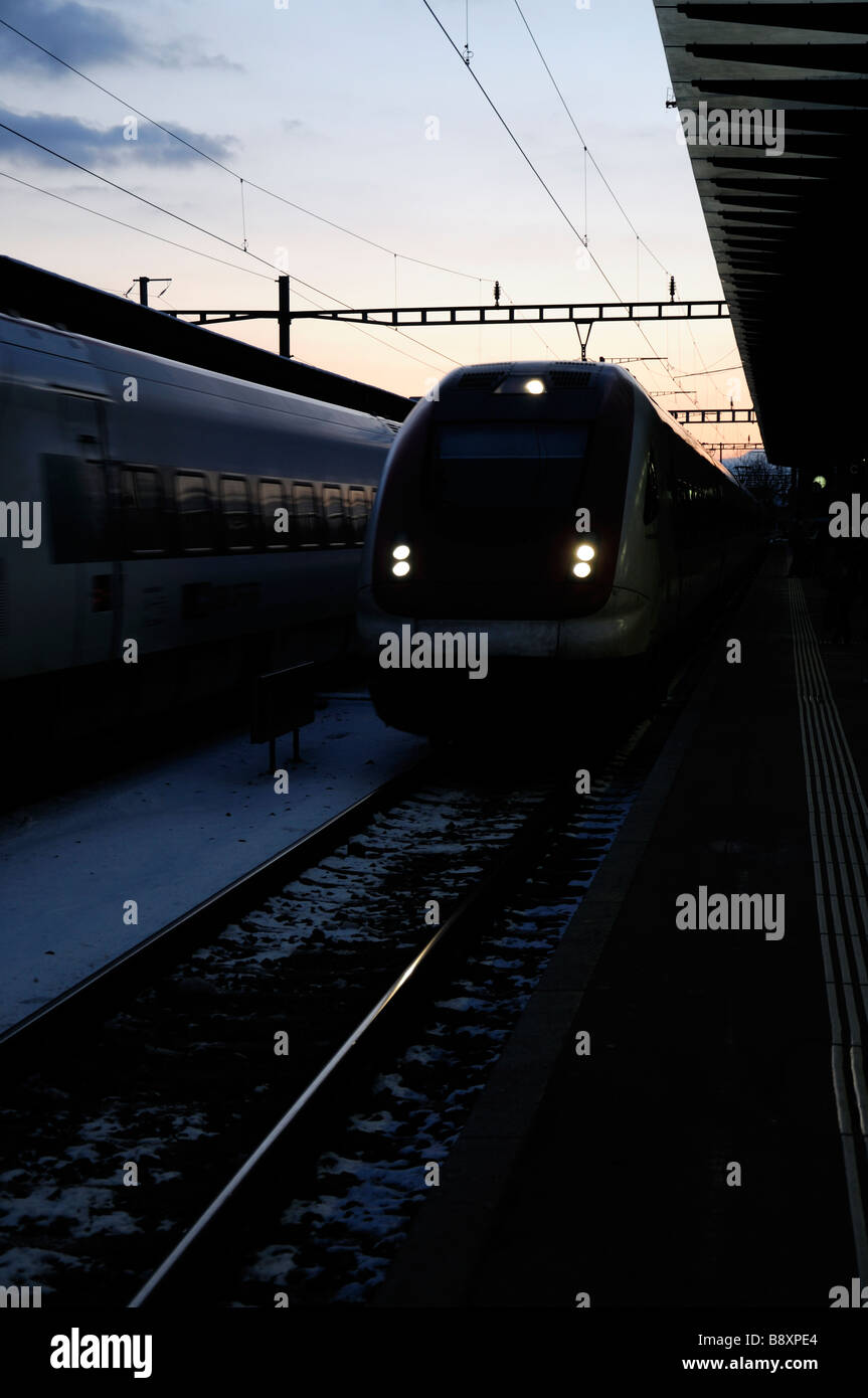 train coming into a swiss switzerland railway station at speed sunset ...