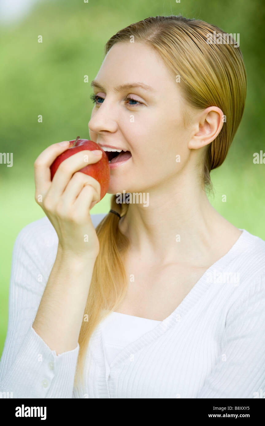 Young woman eating a red apple and looking away Stock Photo - Alamy