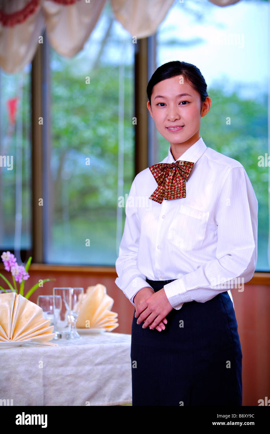 Young waitress well dressed with hands folded in front and smiling at ...
