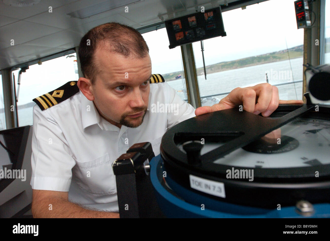 An officer of the Royal Fleet Auxiliary uses a sighting compass on the ...