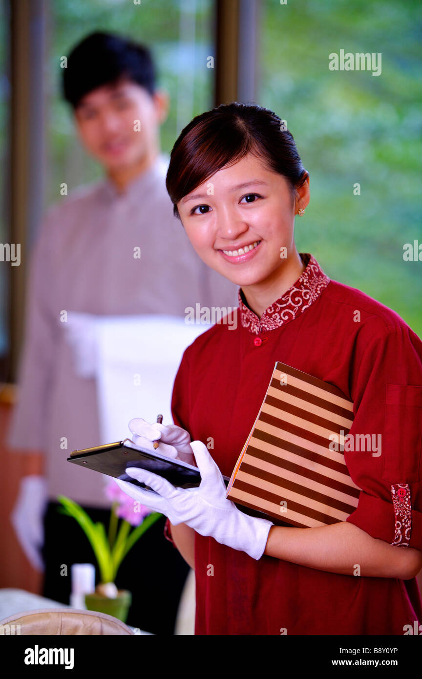 Young waiter and waitress serving and smiling at the camera together ...