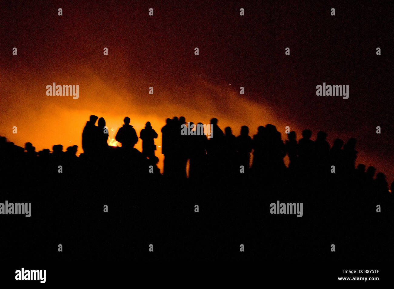 silhouette of crowd of people, behind them the sky is orange and smoky ...
