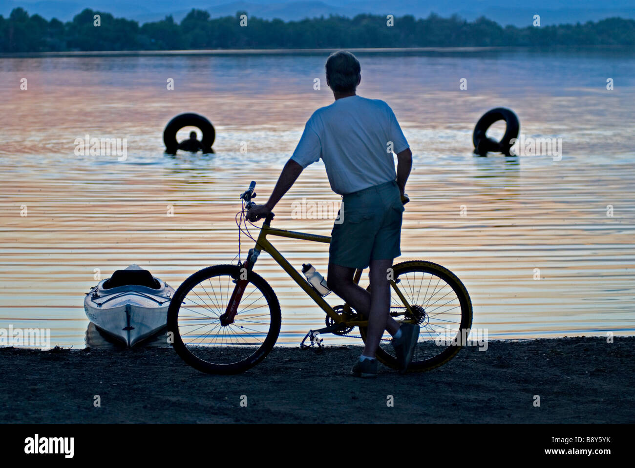 Rear view of a man standing with his bicycle at the lakeside with two ...