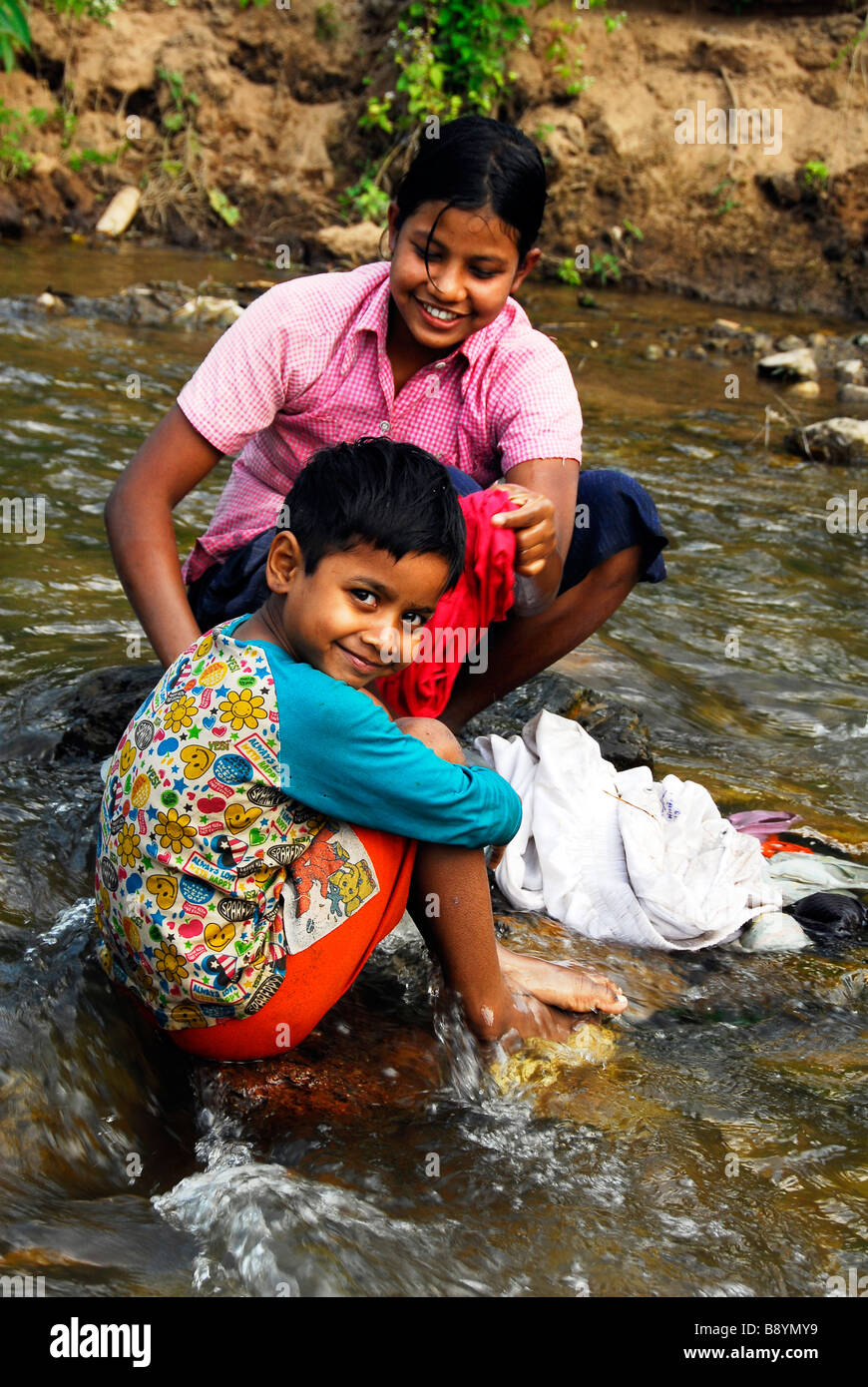 Refugee sister and brother washing clothes in the river near Maela ...