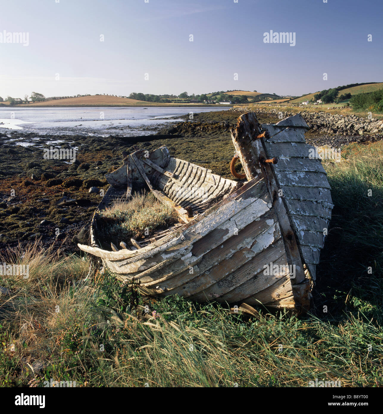 An abandoned and rotting shell of a boat lying on the foreshore of ...