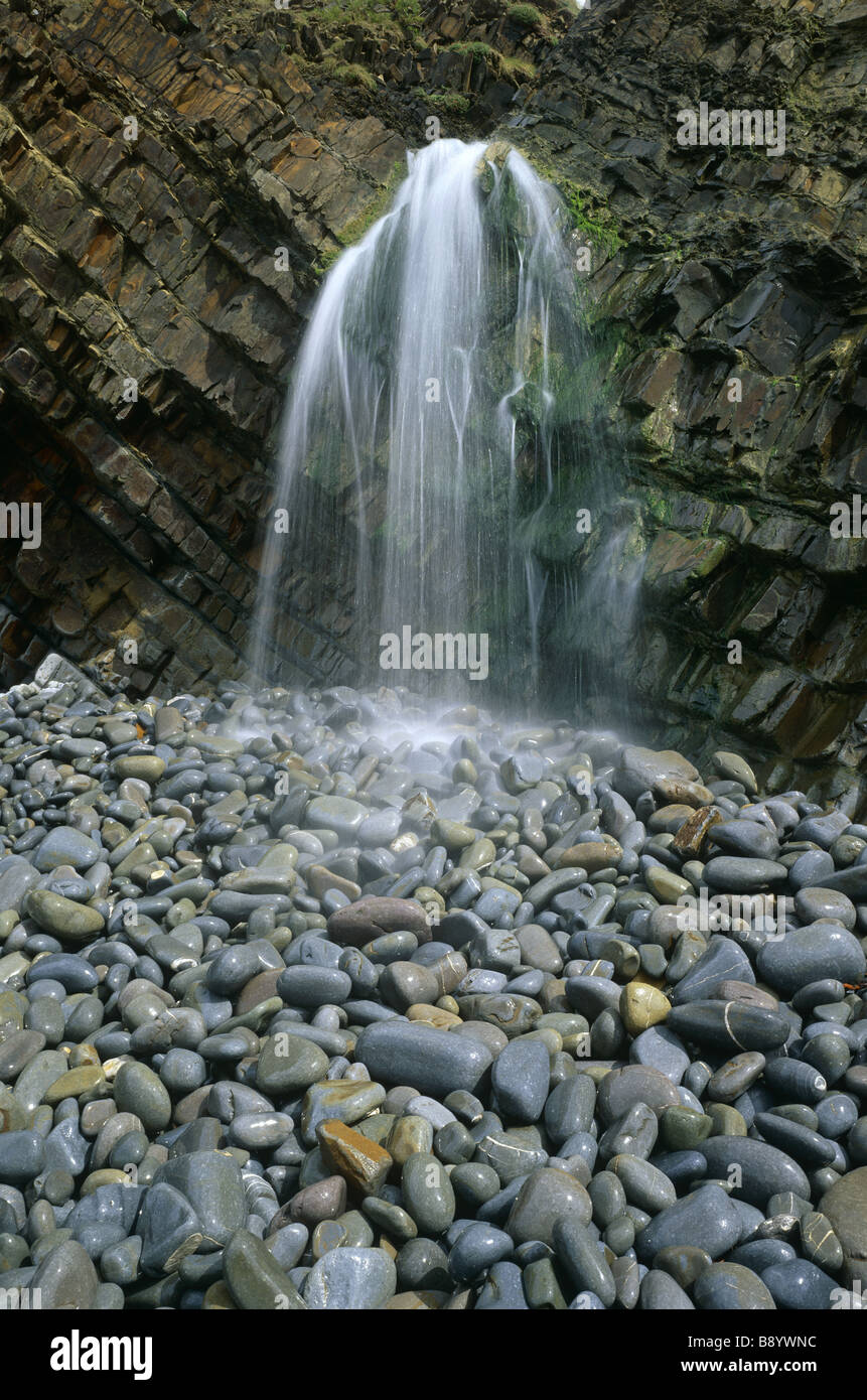 Waterfall and rock strata at Sandy Mouth with smooth wet pebbles in ...