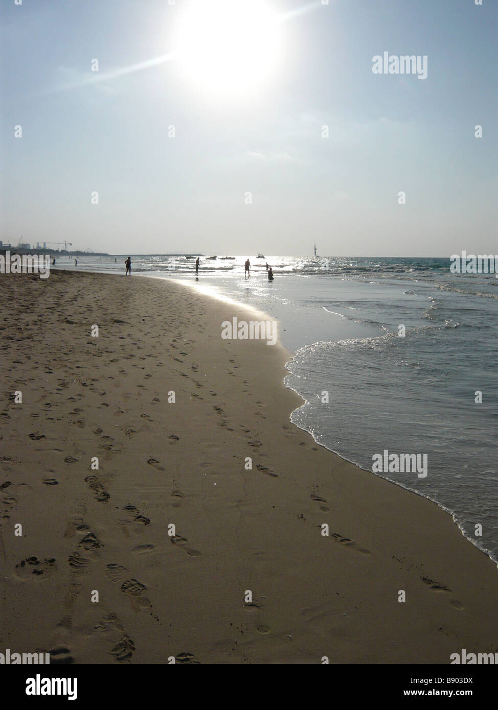 Silhouetted people walking on the shore line with the sun beating down ...