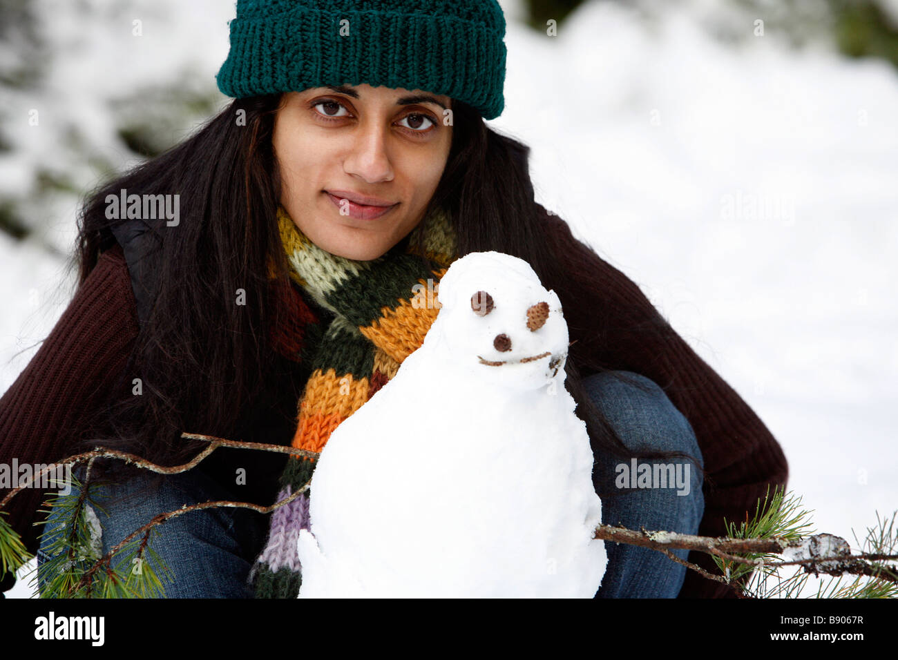 A woman wearing a hat and scarf with a snowman outdoors in the forest ...