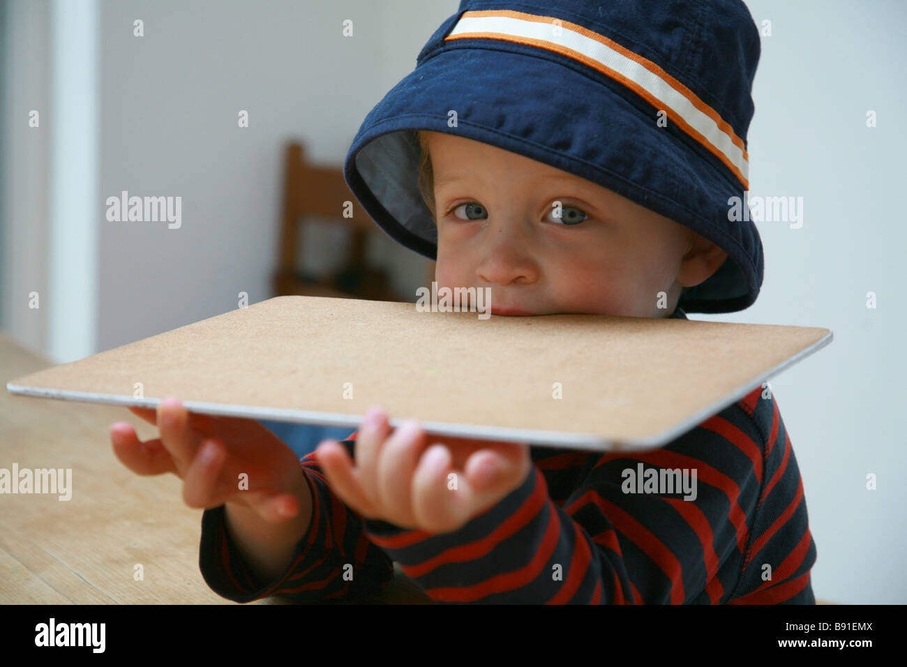 little boy with blue hat bites in table mat Stock Photo - Alamy