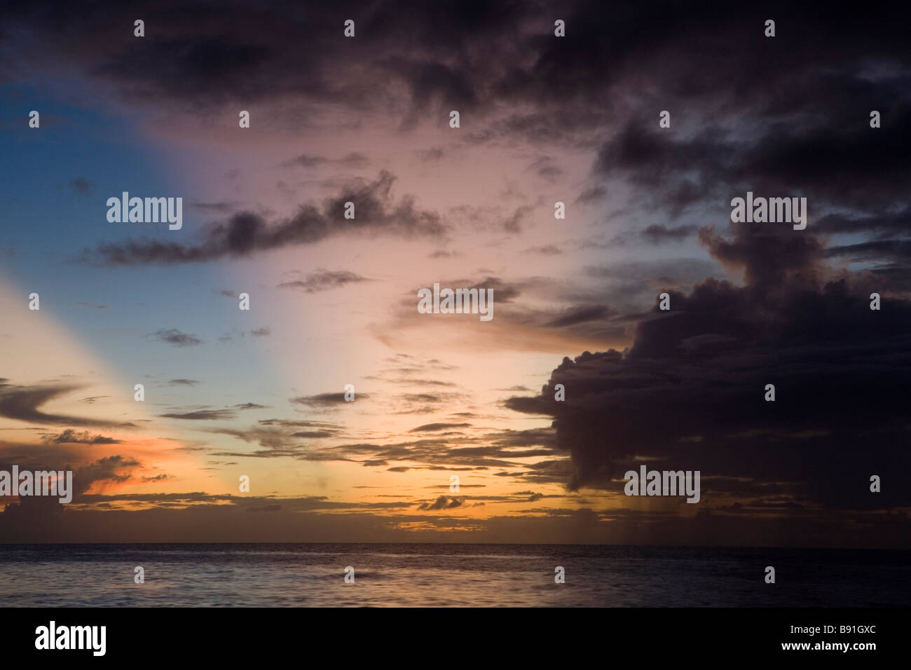Sun setting low over ocean with rain clouds, Island of Tobago ...