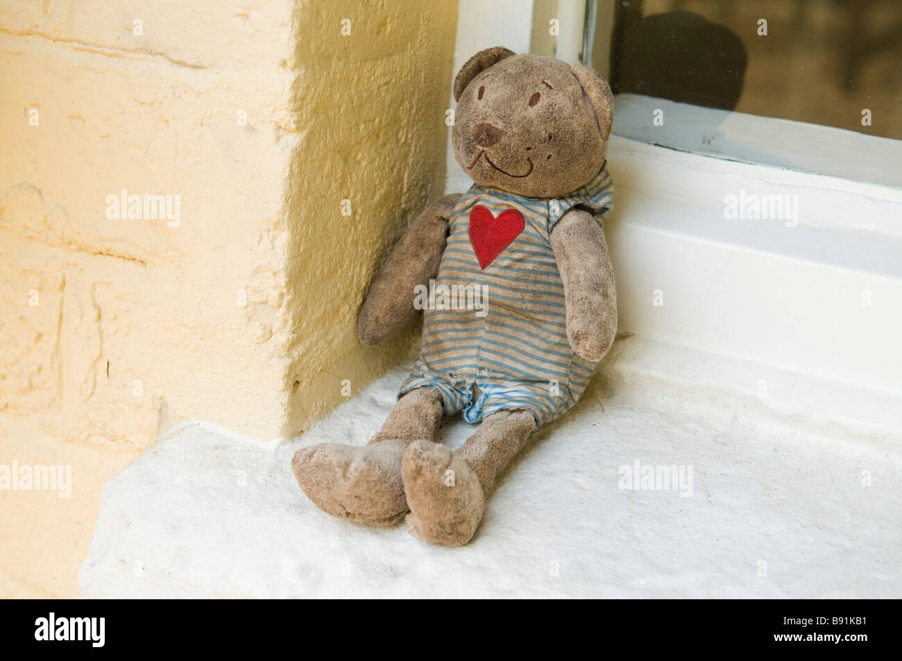 Grubby abandoned teddy bear on a window ledge Stock Photo - Alamy