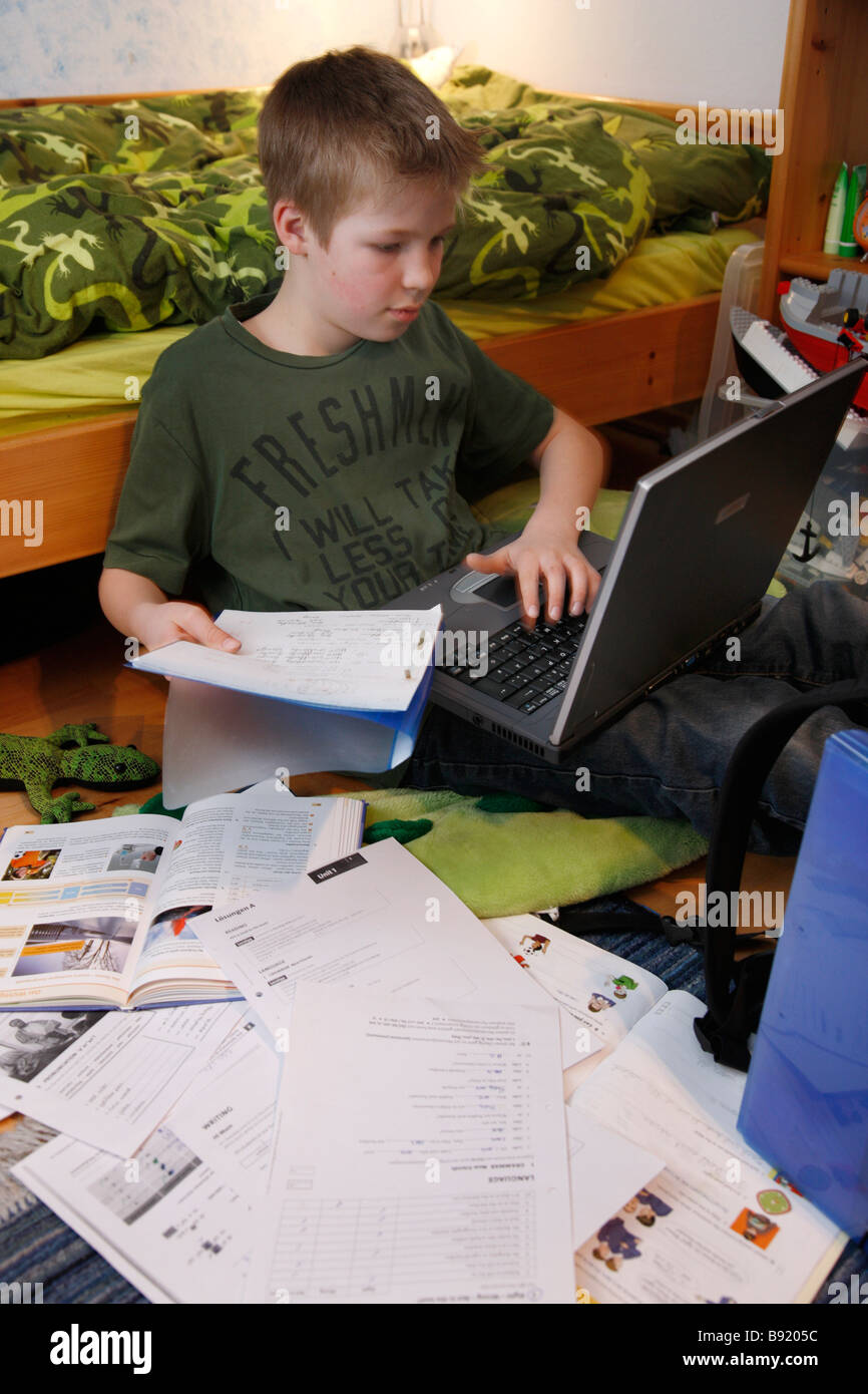A boy, 11 years old, is working at a laptop in his child room. He is ...