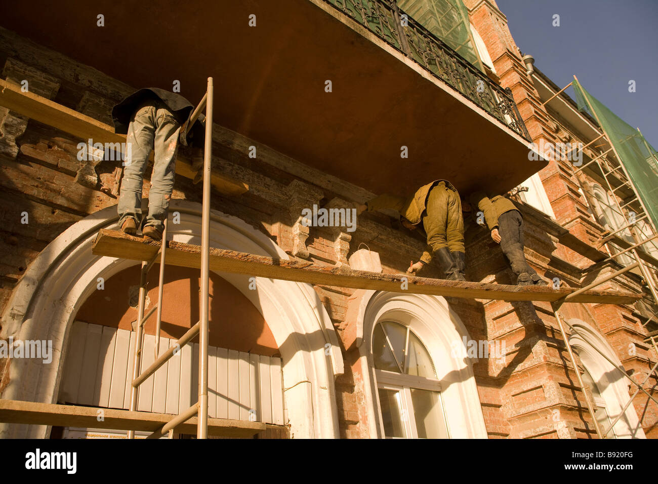 Workmen on scaffolding repairing facade of red brick building ...