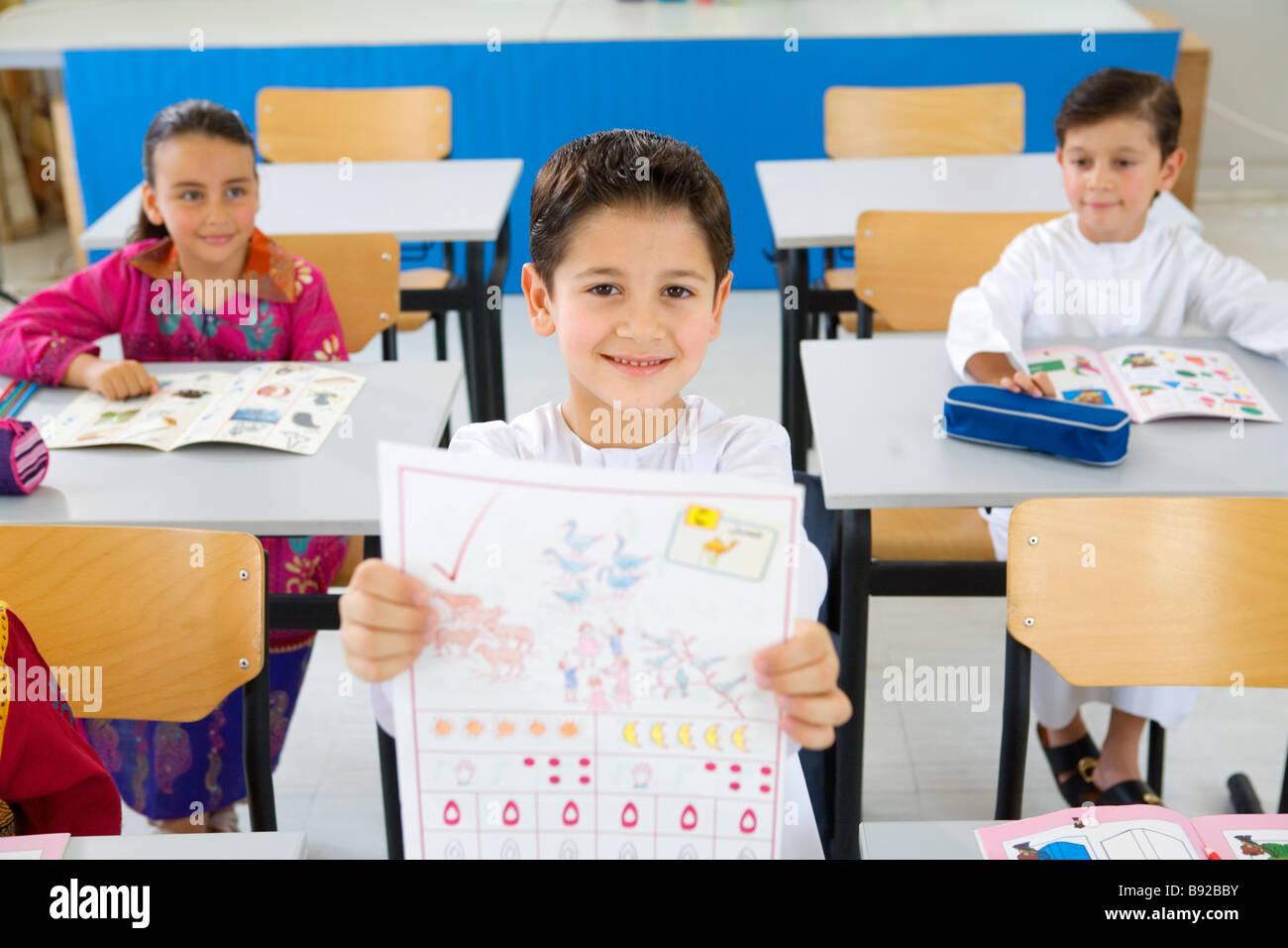 Smiling Arab boy holding up homework in classroom Dubai United Arab ...