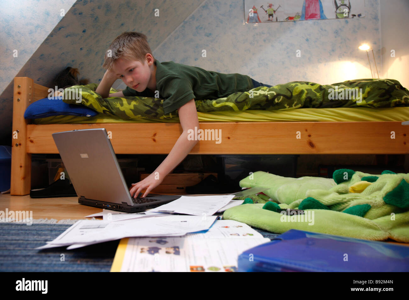 A boy, 11 years old, is working at a laptop in his child room. He is ...