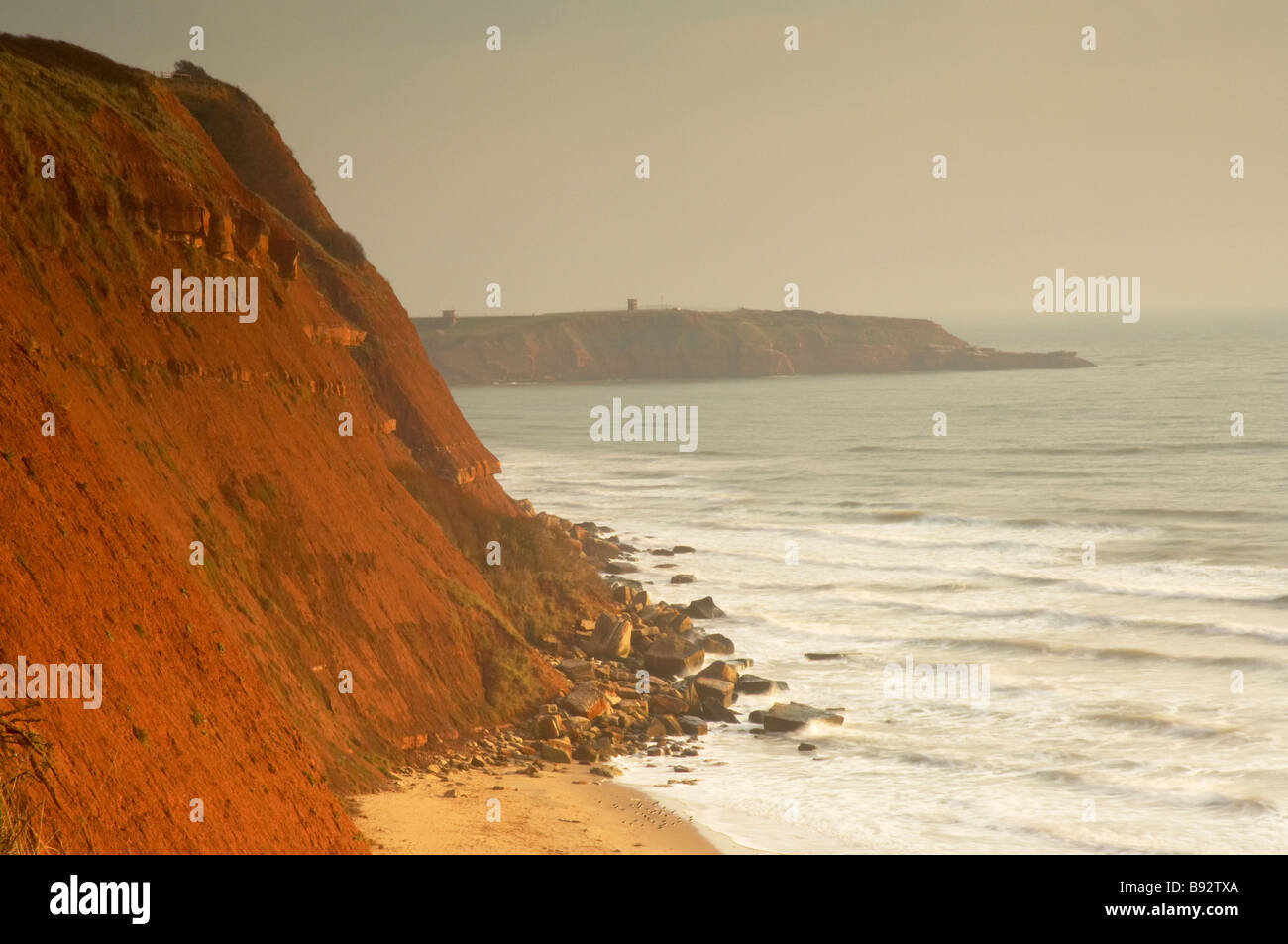 Waves rushing in onto the beach and rockfall below the red sandstone ...
