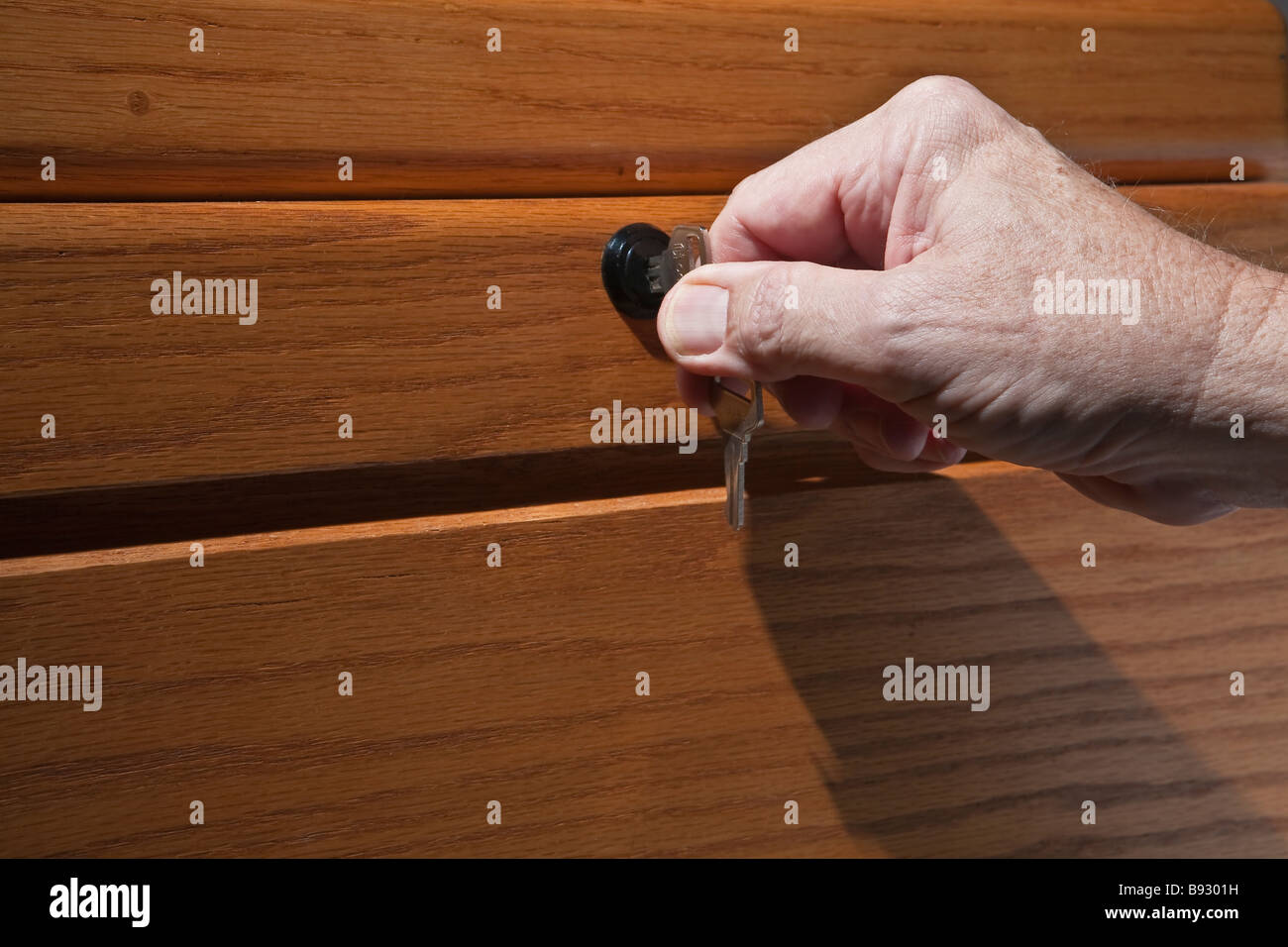 Older man s hand turning key in lock of wooden desk Stock Photo - Alamy
