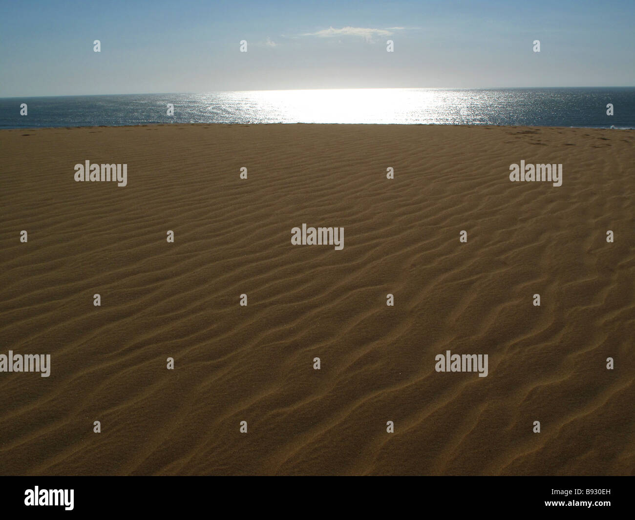 Beach landscape with a sand dune and the sun reflecting over the ocean ...
