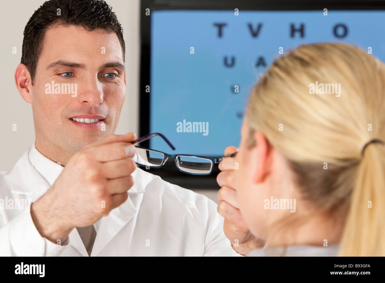 A male optician fitting glasses onto a blond female patient with an ...
