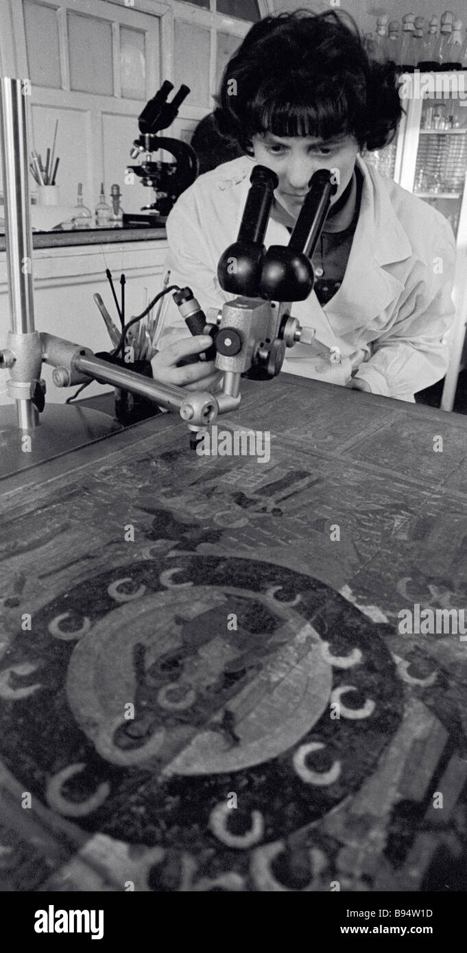 A restorer inspecting under a microscope a Pskov Museum icon sent for ...