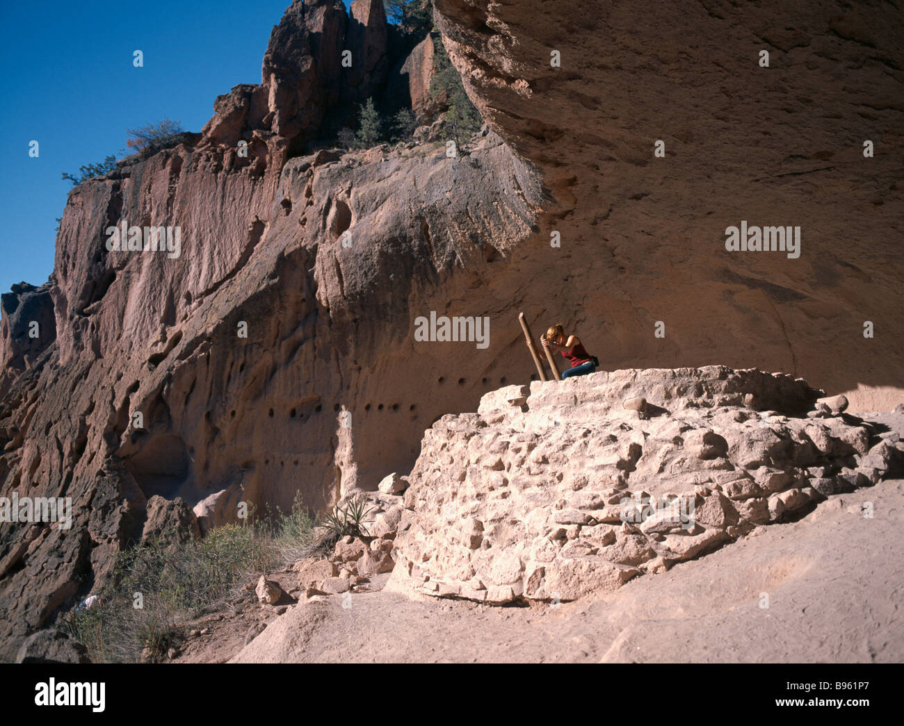 USA New Mexico Bandelier National Monument. Visitor climbing ladder ...