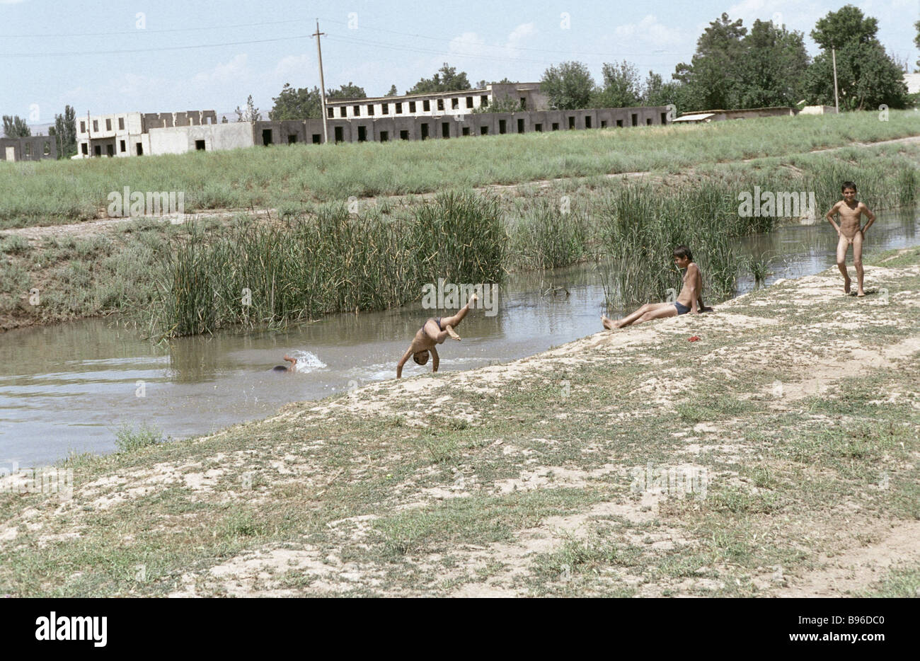 Little boys have a dip in a small irrigation canal in a suburb of ...