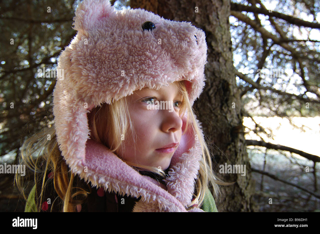 Hiding in a forest tree fort, a girl looks out through the branches at ...