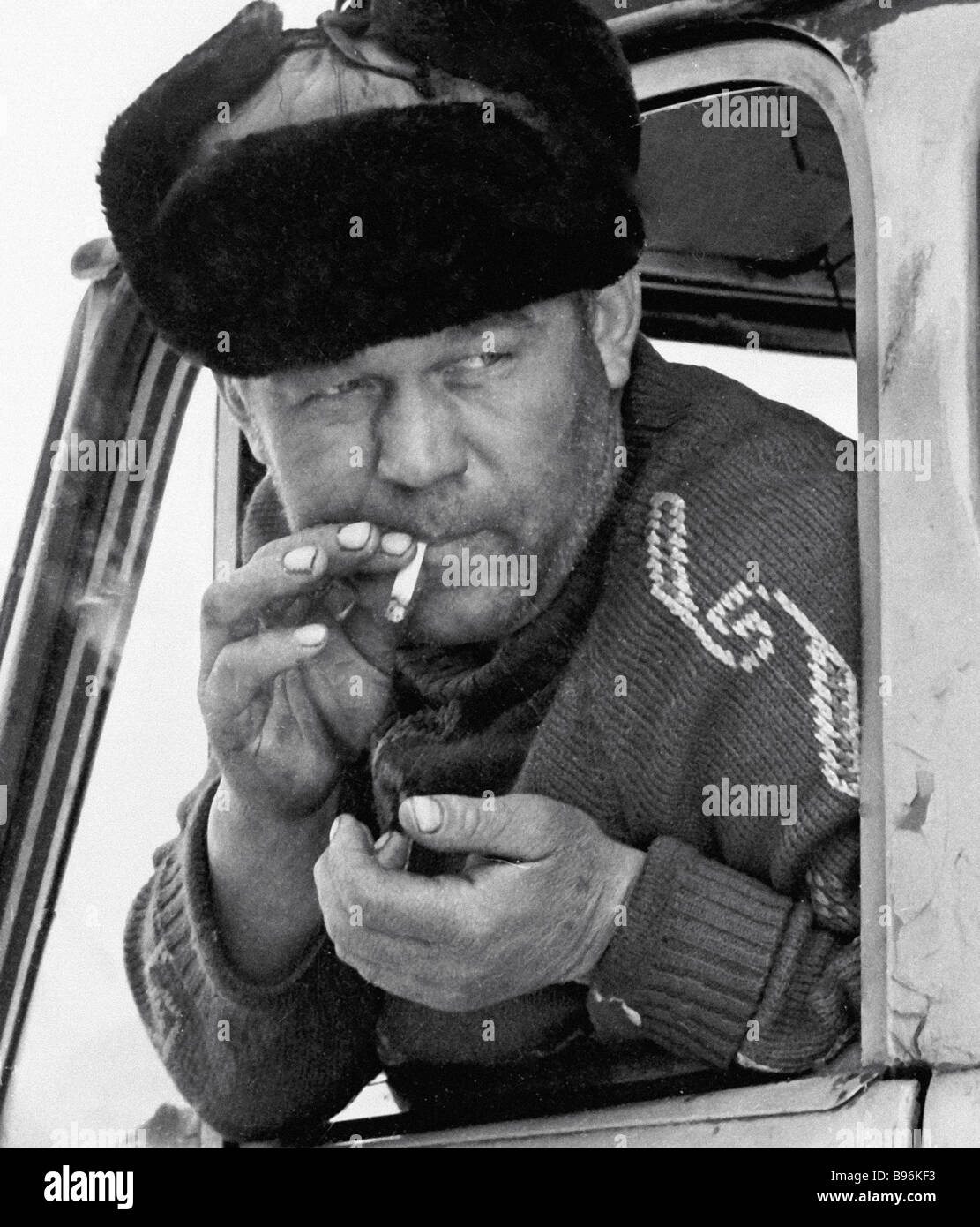 A driver smokes a cigarette poking his head out of the truck window ...