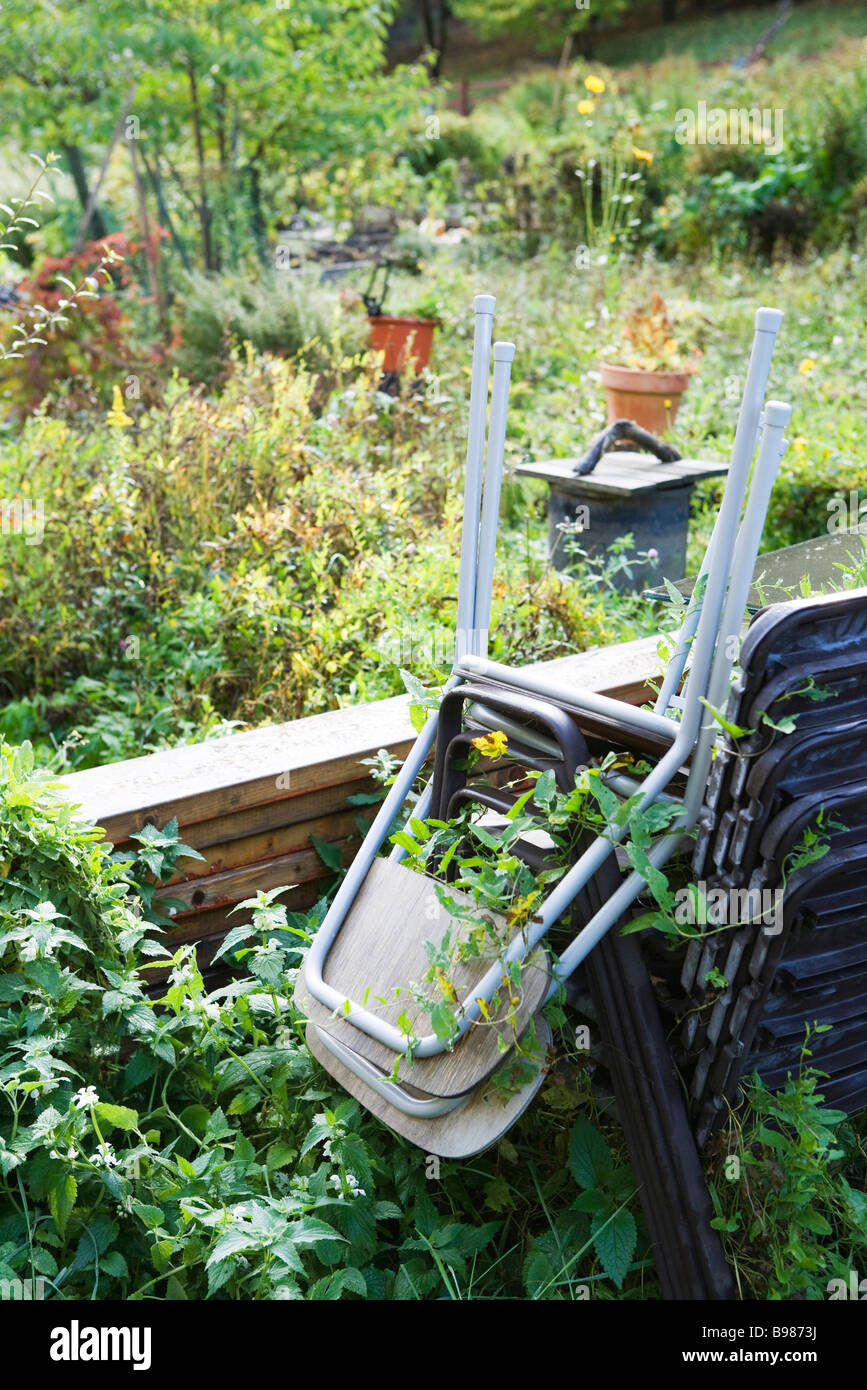 Stack of chairs in overgrown garden Stock Photo - Alamy
