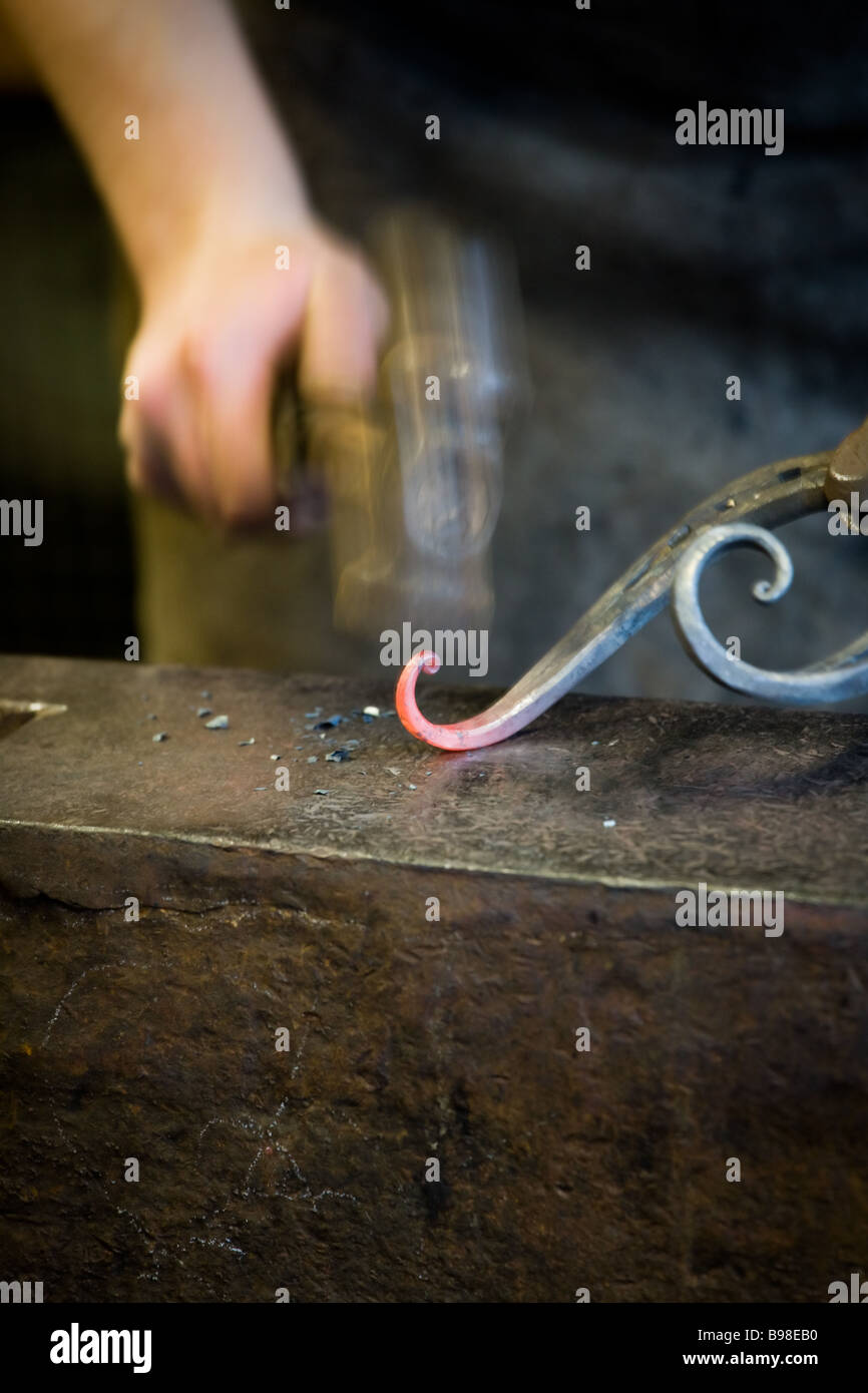 A blacksmith's hammer strikes a piece of red hot ironwork - showing ...