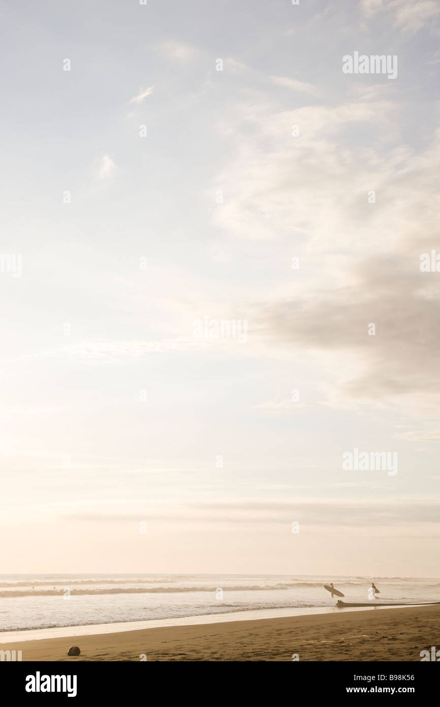 Surfers looking towards the ocean at sunset, Dominical, Costa Rica ...